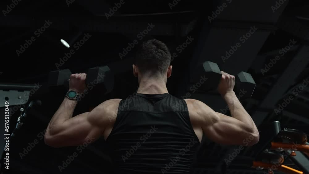 Fit man back view lifting dumbbells over head in fitness gym. Athlete ...