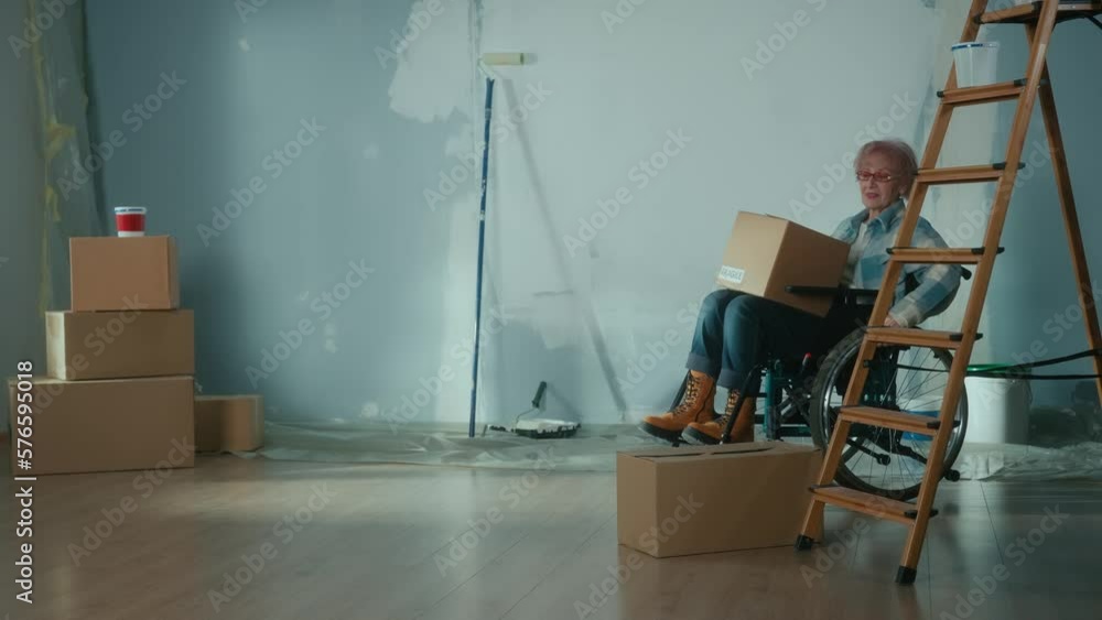 An elderly disabled woman moves in a wheelchair with a cardboard box ...