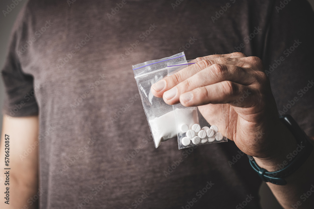Man's hand holds two transparent plastic packets with cocaine powder ...