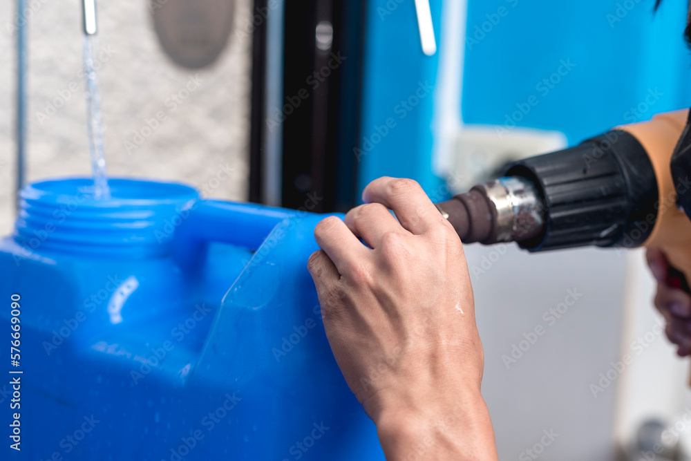 Using a heat gun to tighten the plastic seal on the cap lid of a blue ...