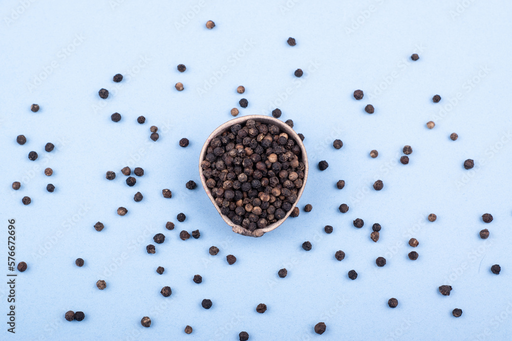 Wooden bowl with black pepper scattered around—a wooden bowl filled ...