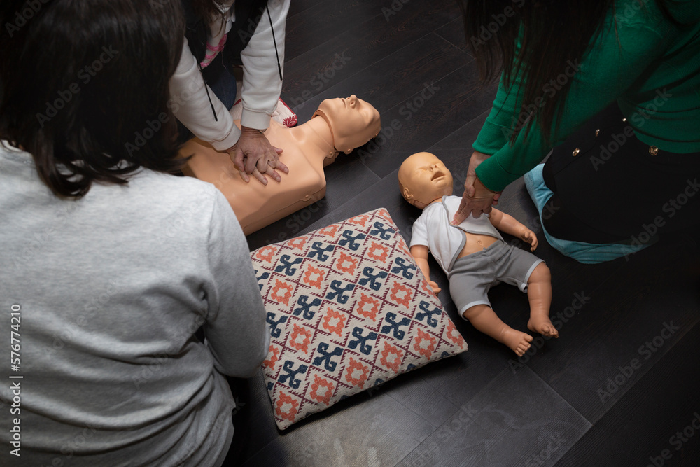 Three people practice first aid and CPR with an adult CPR manikin and ...