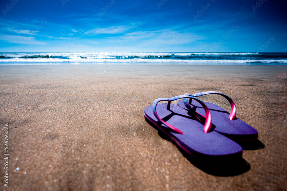 Horizontal photo of purple sandals on the sand in front of the waves of ...