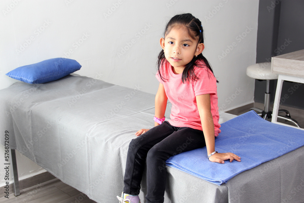 Foto de 4-year-old brunette Latina girl sitting on the bed in a doctor ...