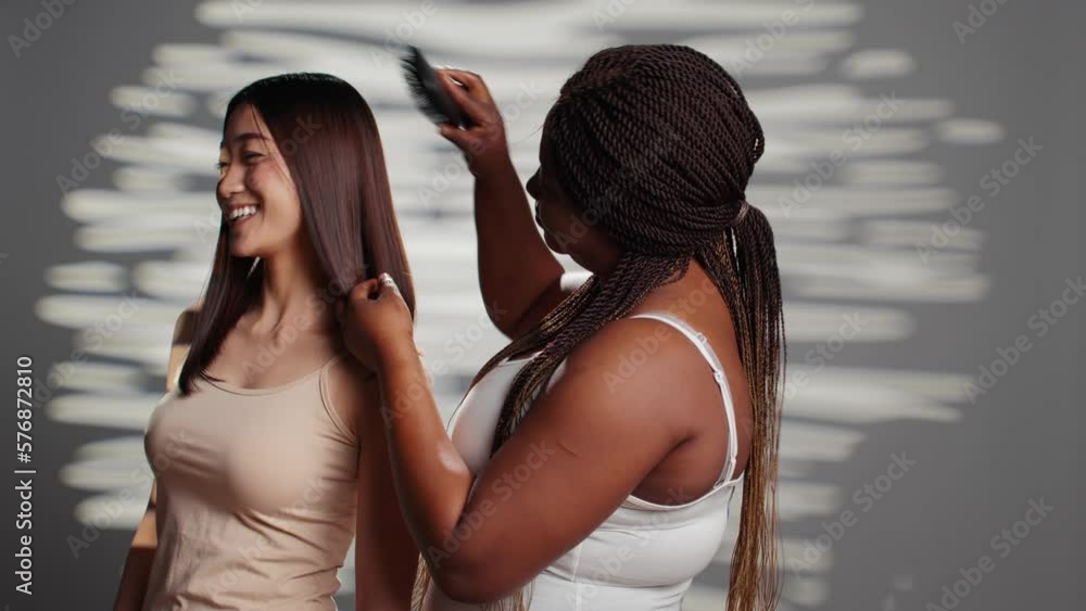 Interracial women advertising friendship in studio, curvy girl brushing ...