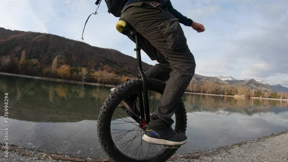 Man lower body (legs and foot) riding a unicycle on lake shore in ...