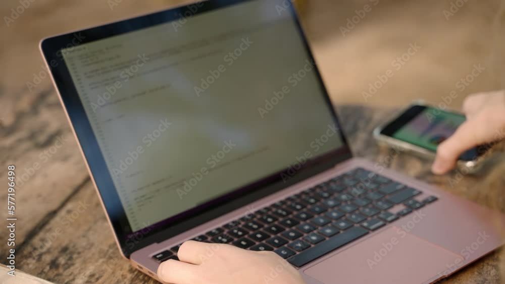 Woman developer working on laptop takes phone with diagrams and checks ...