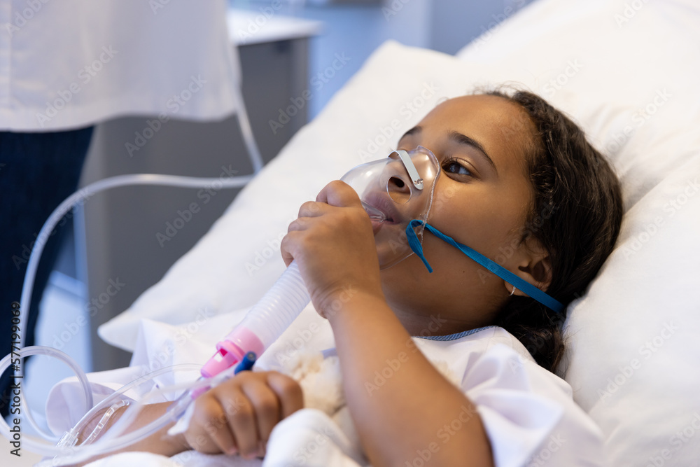 Sick biracial girl with oxygen mask and teddy bear on hospital bed ...