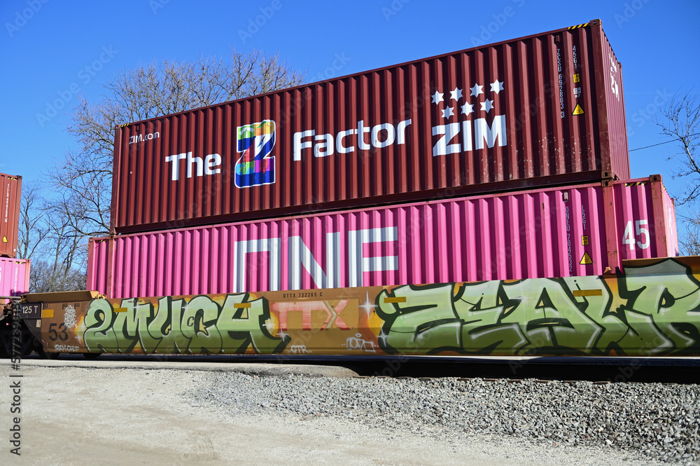 Colorful intermodal freight containers carried in a graffiti-clad well ...