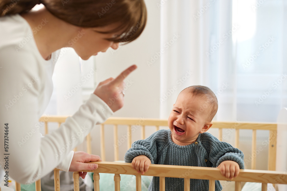 Little baby boy crying in the crib while his mother pointing finger and ...
