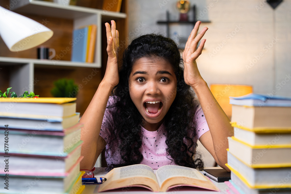 Shouting or screaming young girl in front of stack of books on study ...