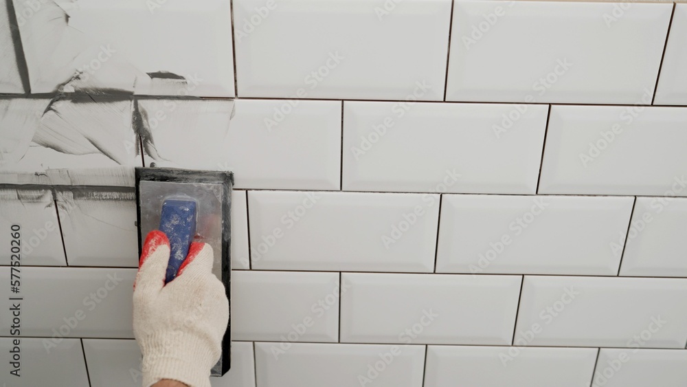 Workers' hands using a rubber spatula and grouting with paste between ...