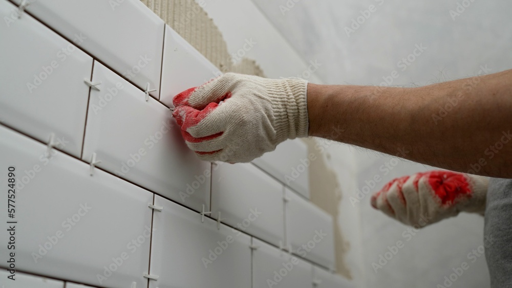 Workers lay ceramic tiles on the kitchen wall. Construction details ...