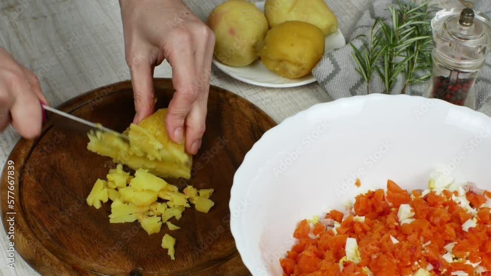 A housewife cuts boiled potatoes with a kitchen knife on a wooden ...