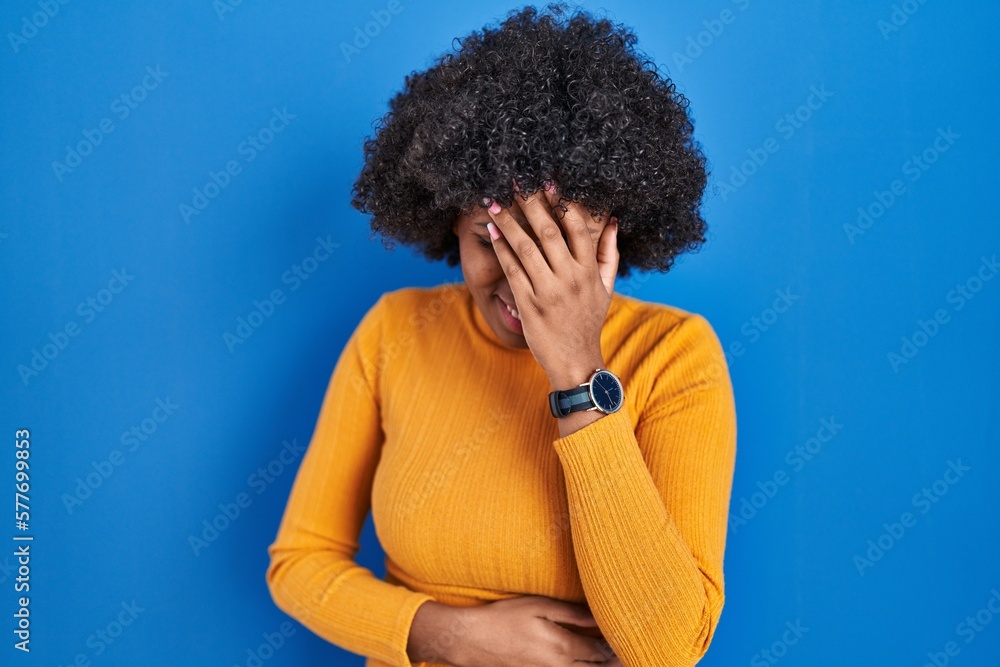 Black woman with curly hair standing over blue background with sad ...