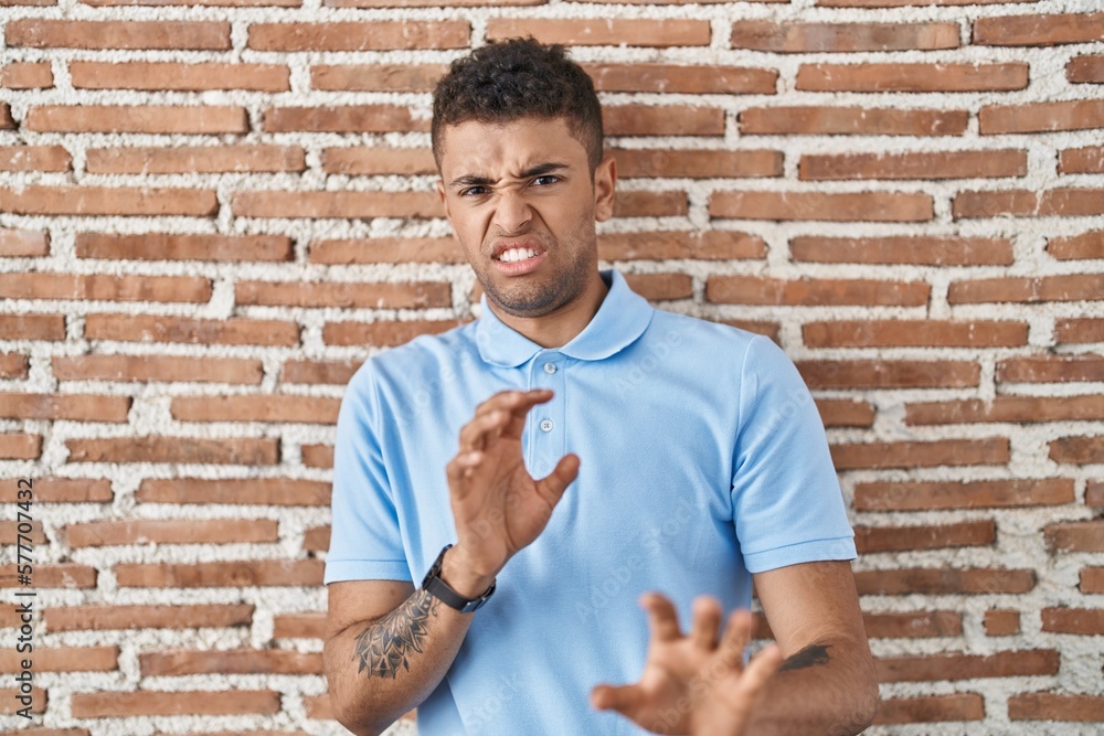 Brazilian young man standing over brick wall disgusted expression ...