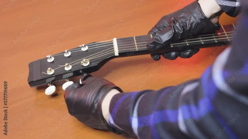 man with guitar,master hands in gloves puts on new strings and tuning ...