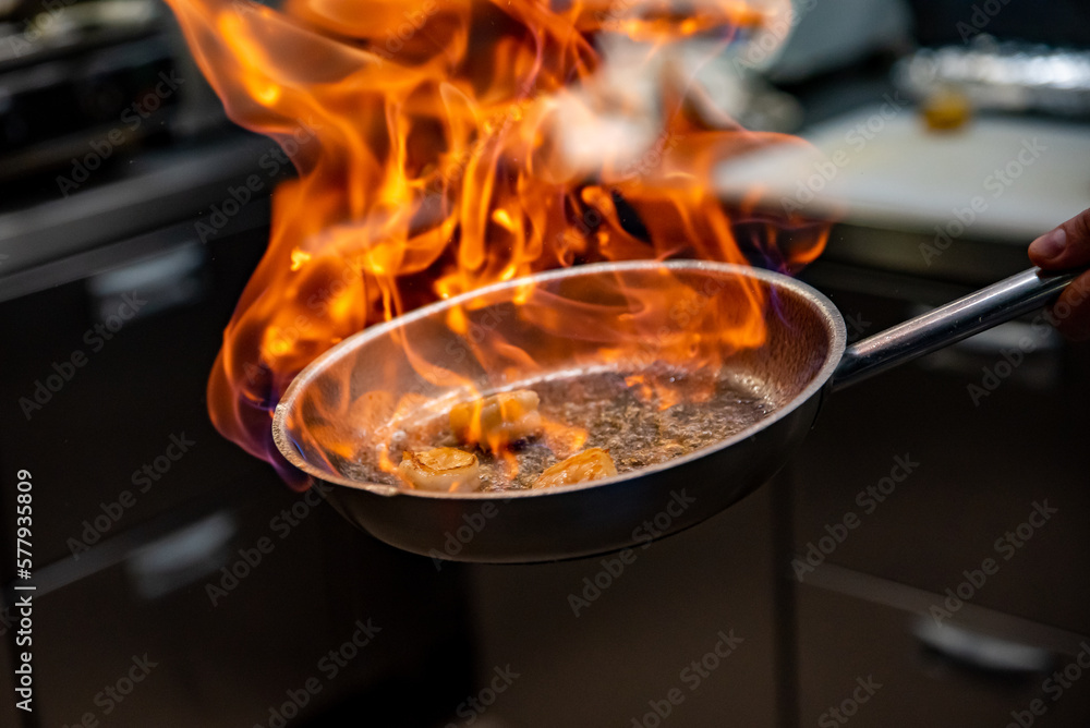 Chef hand in restaurant kitchen with pan, cooking flambe on shrimps ...