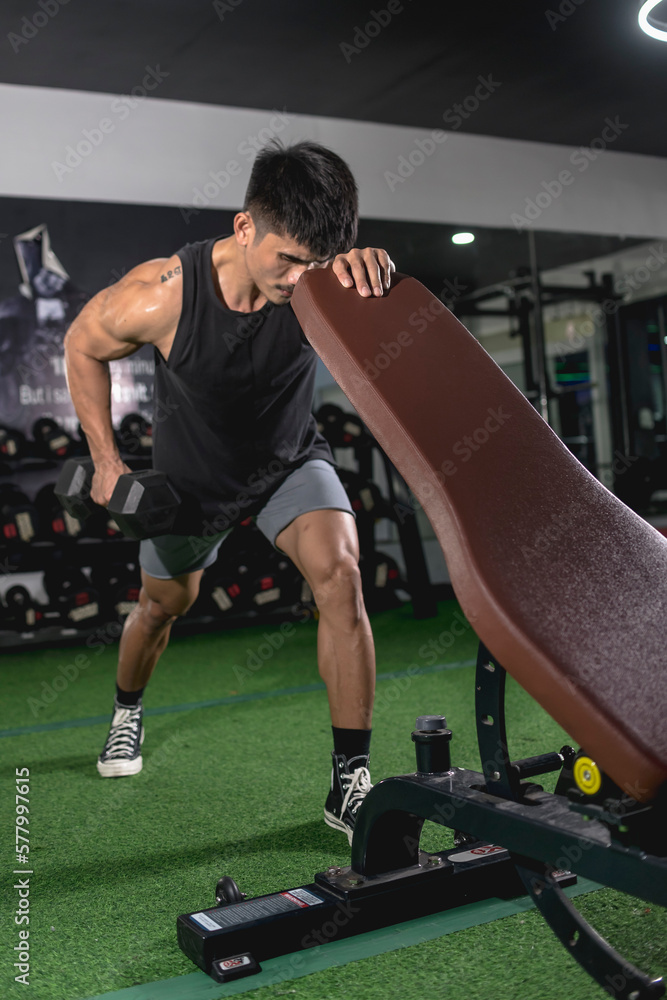 A determined man does one-arm dumbbell rows while leaning on an incline ...