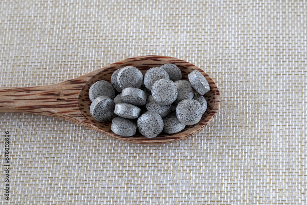 Round brown tablets with spots on a beige background in a wooden spoon ...