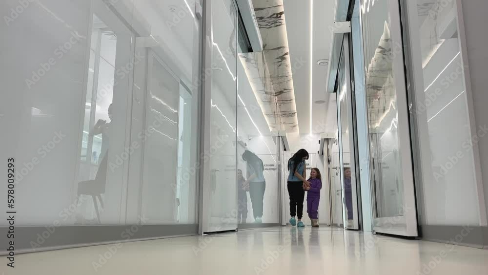 woman and girl walk along corridor look at each other large white hall ...