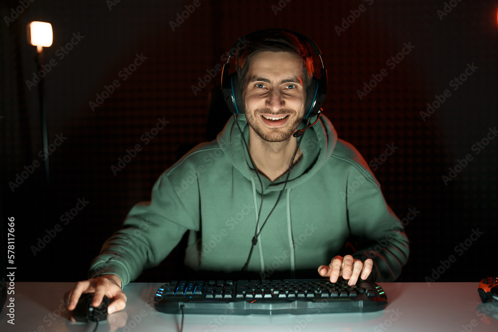 Smiling young male cybersport gamer in hoodie and headset using ...