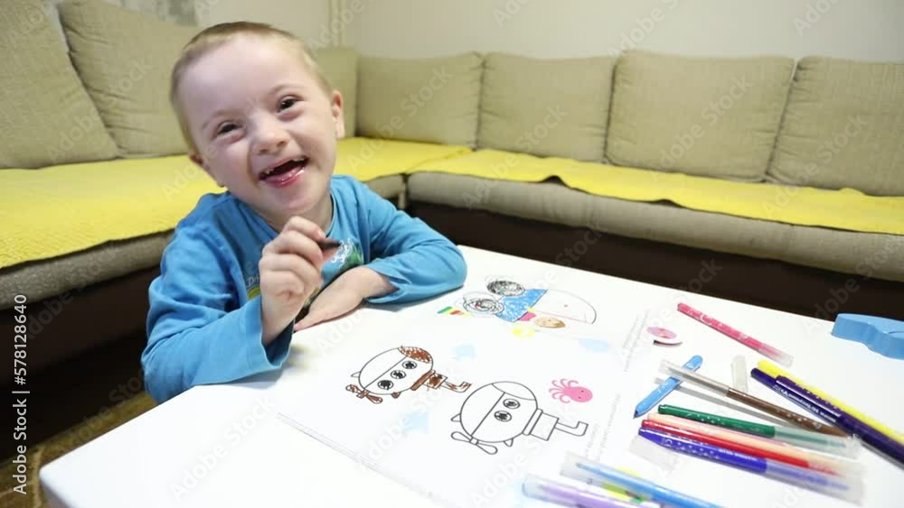 Cute young boy laughs while working on his drawing. People with Down ...