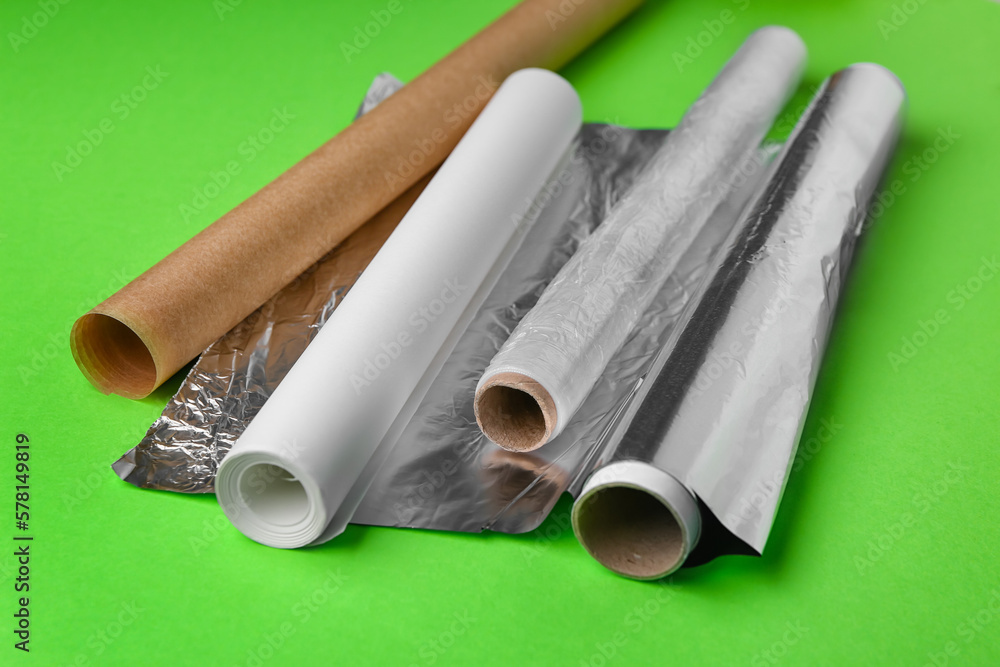 Rolls of aluminium foil, baking paper and food film on green background ...