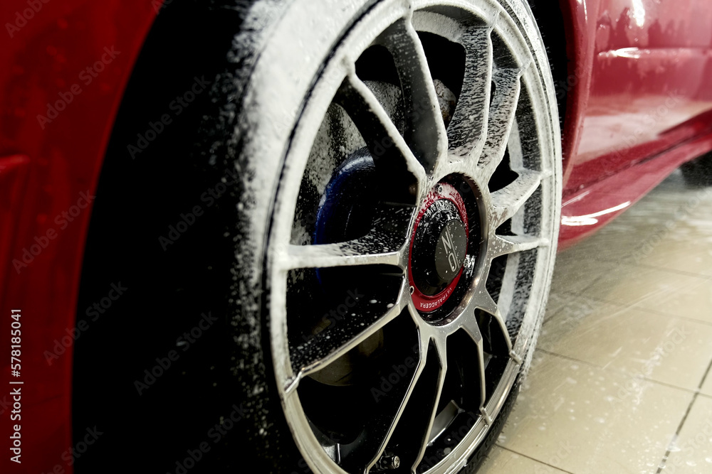 Man washes a red Subaru at a car wash. Close-up of car wheels with OZ ...
