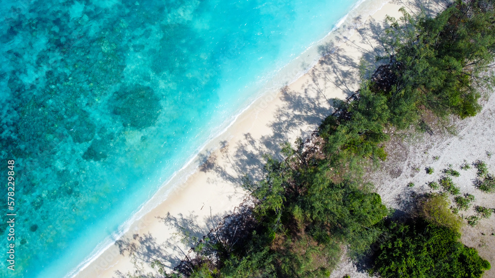 Aerial birds eye view of remote tropical island with crystal clear turquoise ocean water lapping ...