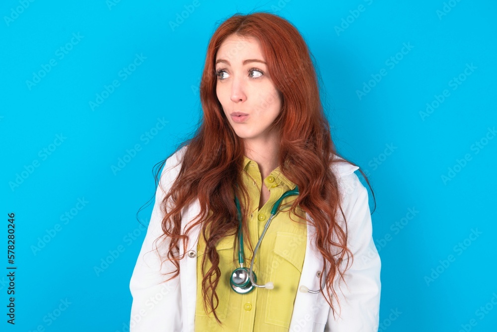 Shocked young doctor woman wearing medical uniform over blue background ...