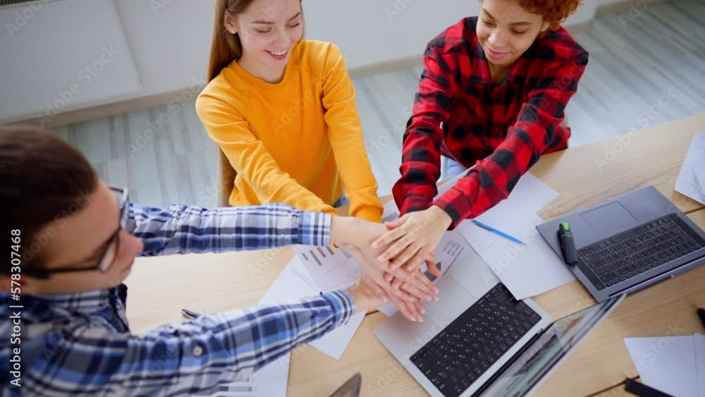 Colleagues put hands together on top of each other, say motto ...