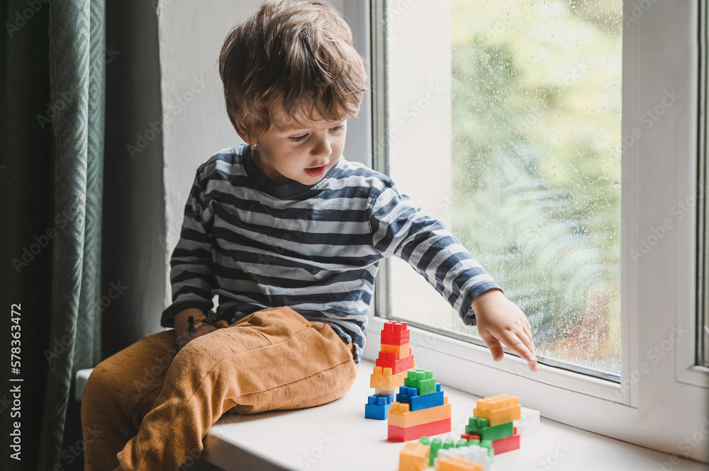 Little boy sitting on the window sill and playing with lots of colorful ...