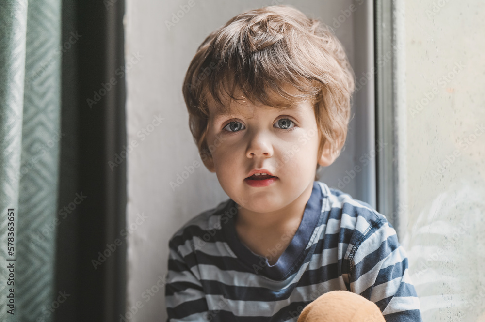 Portrait of little boy sitting on the window sill. Boy playing with ...