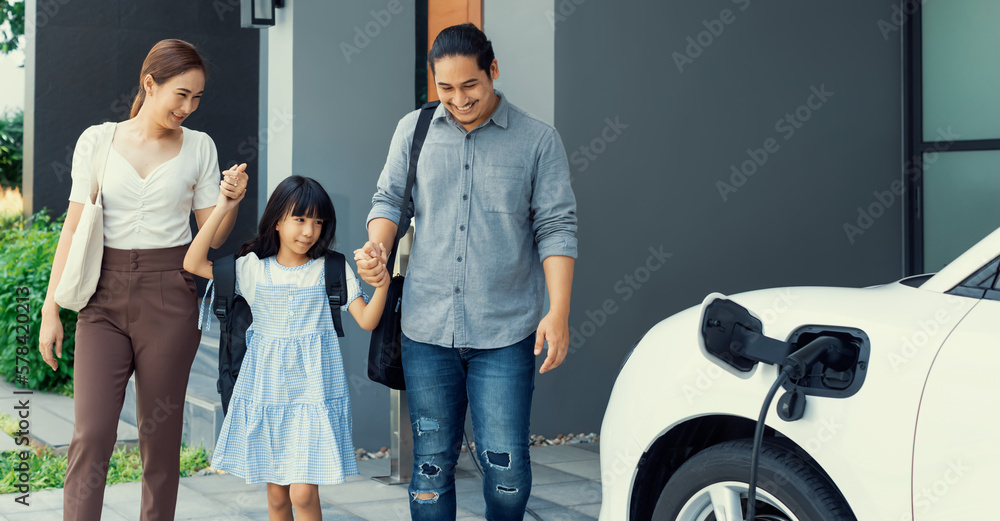 Progressive young parents and daughter with electric vehicle and home ...