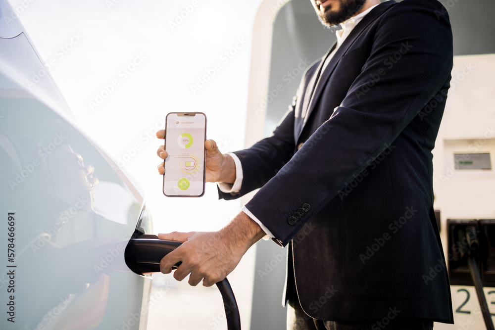 Crop of man in black suit plugging power cord and showing mobile screen ...