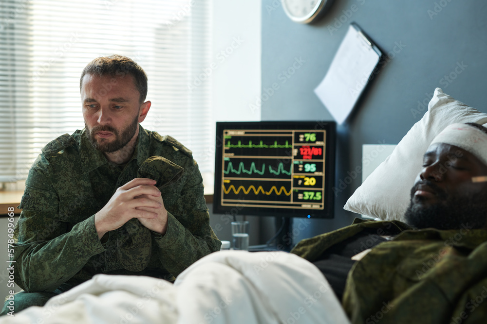 Young soldier in military uniform sitting by bed of African American ...