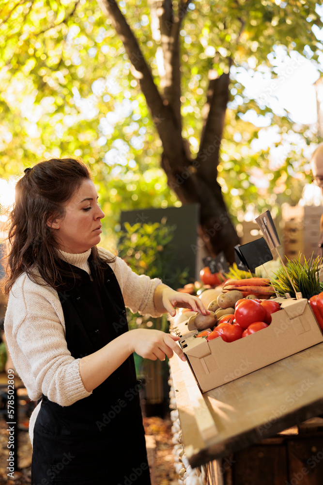 Woman vendor arranging fresh organic produce on stall, putting ...