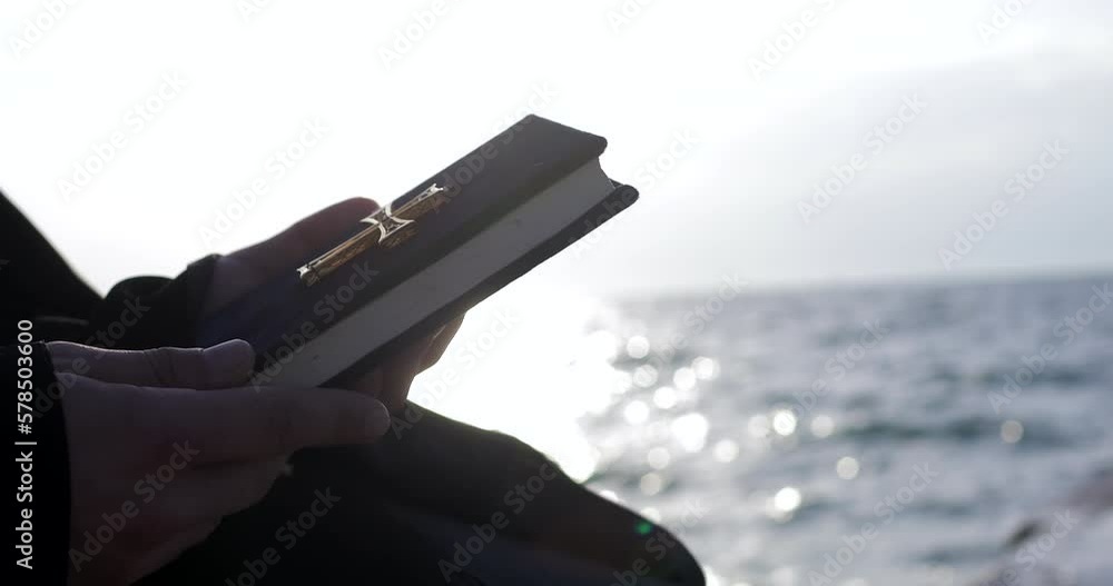 Priest hold a book with a cross on the cover and prays, background of ...