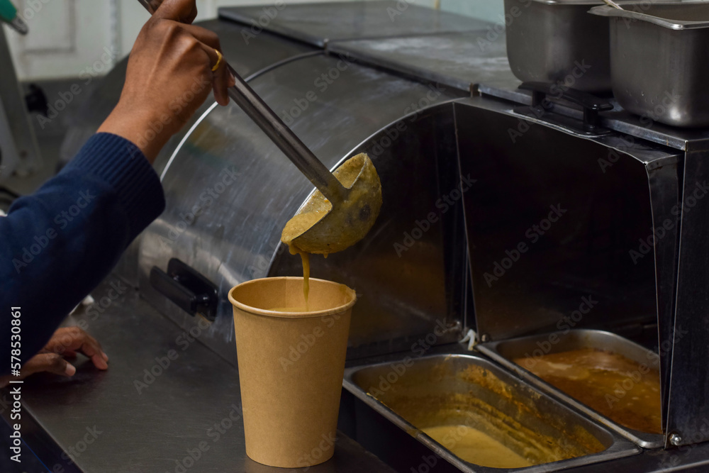 Restaurant kitchen employee pouring soup into a take out paper ...