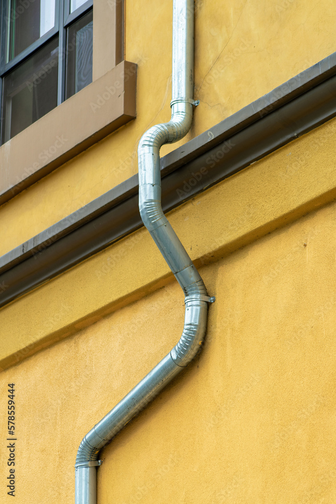 Bending gray metal rain gutter on side of orange stucco cement building ...