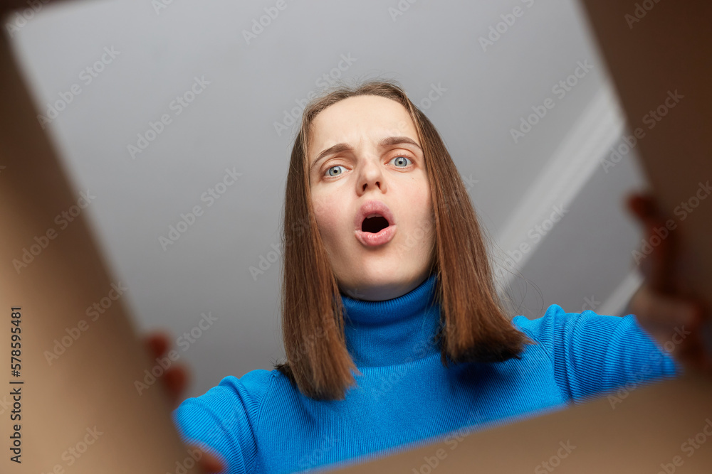 Shocked disappointed woman customer wearing blue turtleneck opening ...