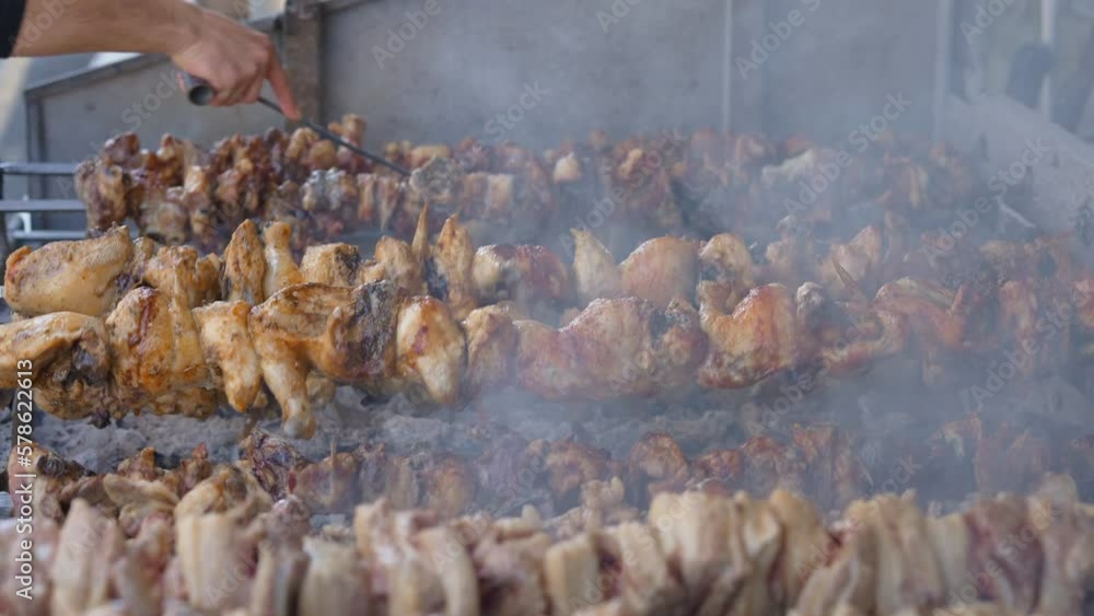 Skewers with meat rolling outdoors with female hand adjusting coals ...