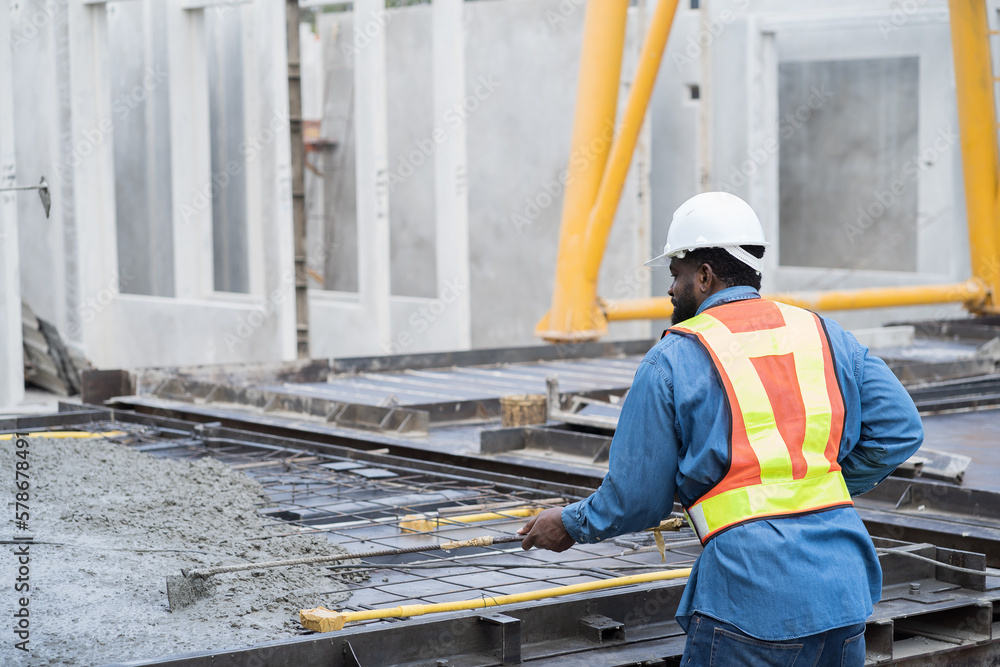 Construction worker uses long steel trowel spreading wet concrete ...