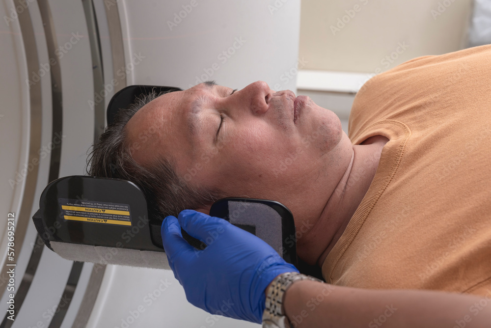 A CT Technologist positioning the head of a male patient on a holder or ...