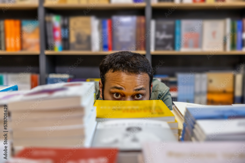 Young dark-skinned man hiding behind the bookshelves Stock Photo ...