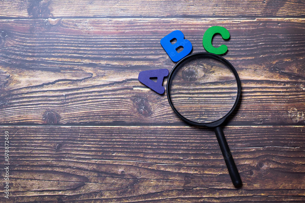 Multicolored English letters spread on the wooden floor. Magnifier and ...