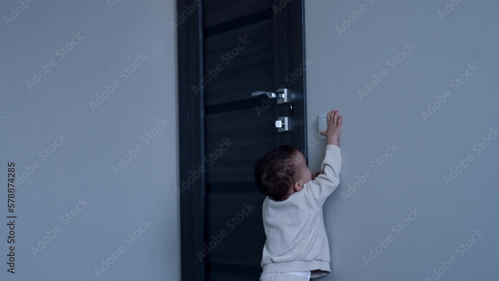 Toddler boy walks up to a light switch. Baby switches the light on ...