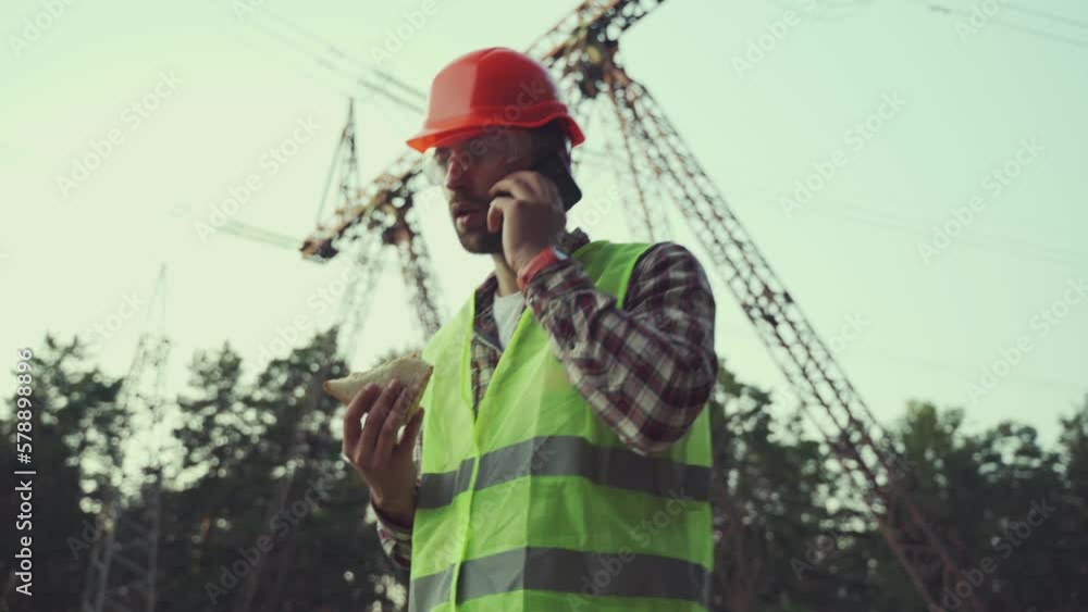 Man working on power line eating sandwich and talking on phone at lunch ...