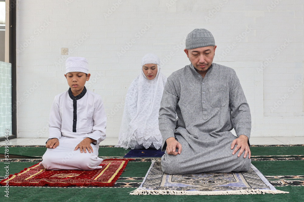 Asian muslim family praying salah jamaah together at home, last movement on salat procedure. The ...